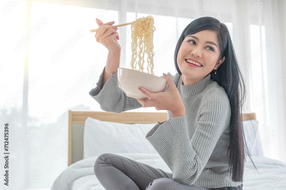 Beautiful asian woman eating chicken instant noodles soup in bed. Girl ...