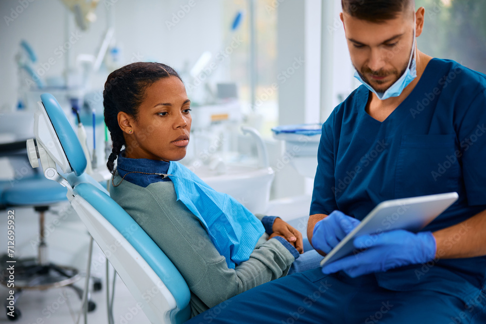 Black woman and her dentist using touchpad during dental procedure ...