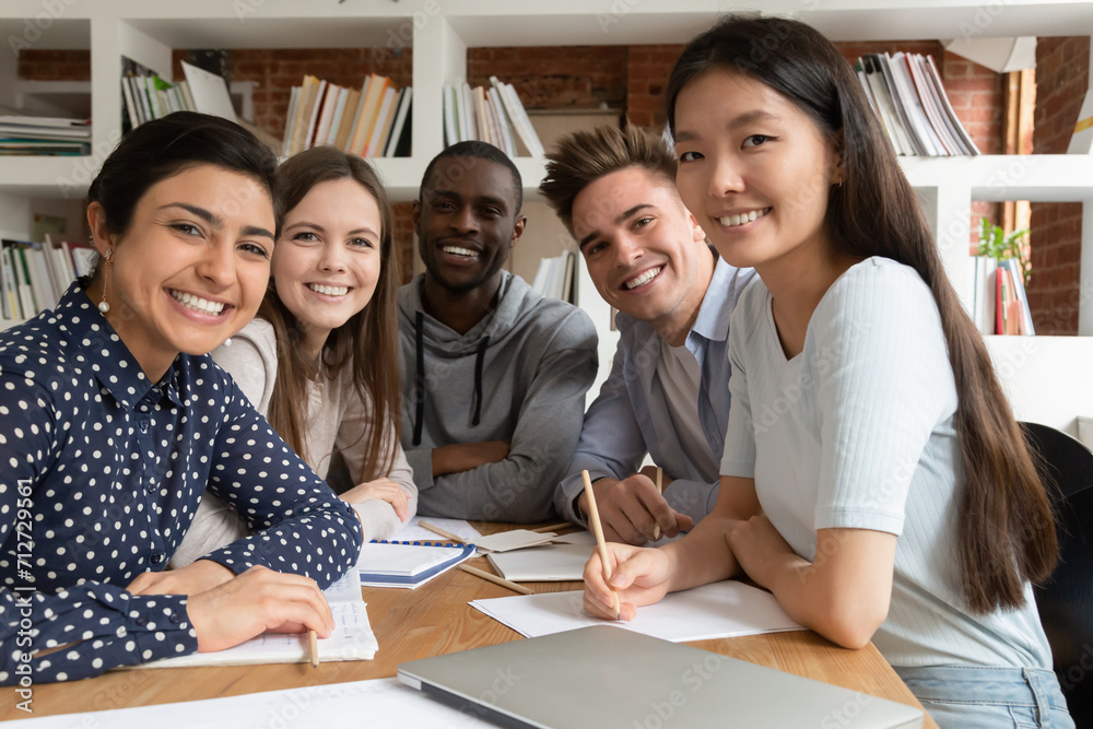 Smiling multiethnic students sit at desk working studying in classroom posing for group picture ...
