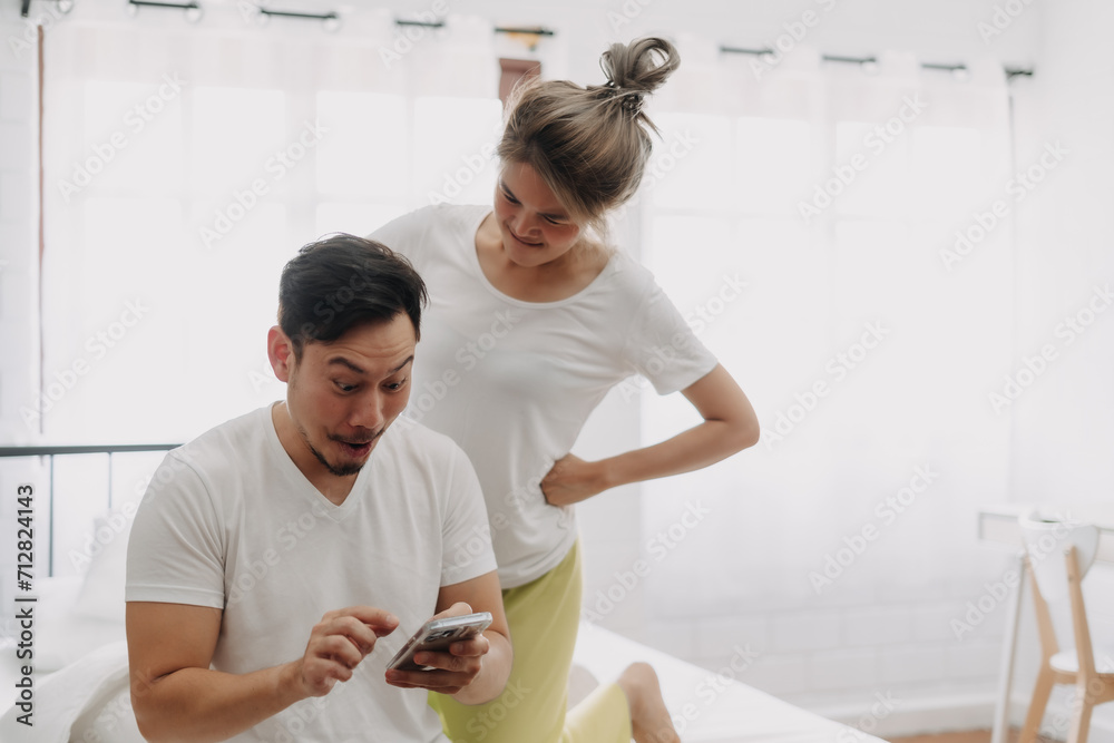 Funny asian couple. Wife peeking husband who chatting on the smartphone. Stock Photo | Adobe Stock