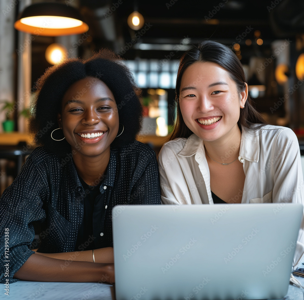 two woman smiling working collaboratively on laptop computer, in the ...