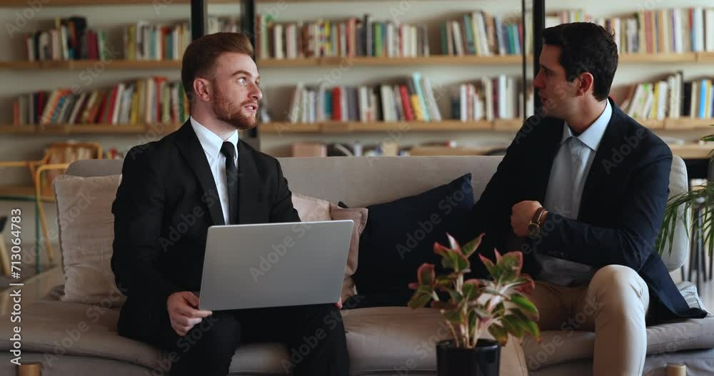 Two colleagues talking seated on sofa in office hallway. Multiethnic ...