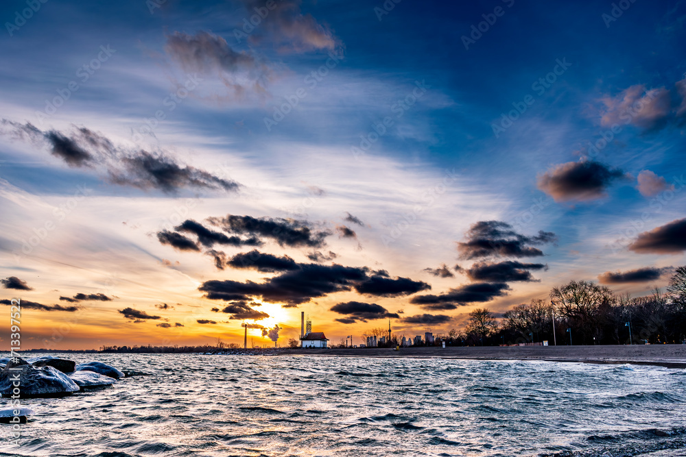 sunset on icy beach in winter with dramatic clouds and downtown skyline ...