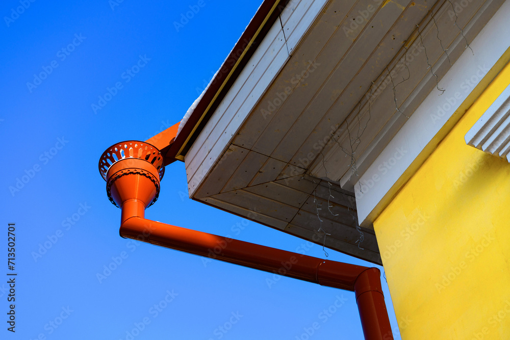 Corner of a yellow house with roof and red pipe.Metallic gutter system ...