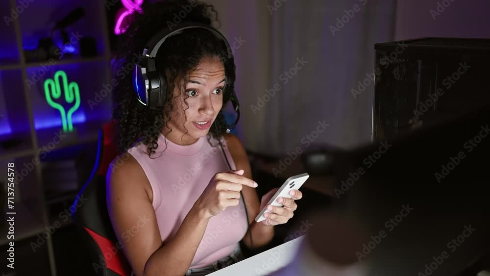 Stunning young hispanic female gamer streaming, speaking on smartphone ...