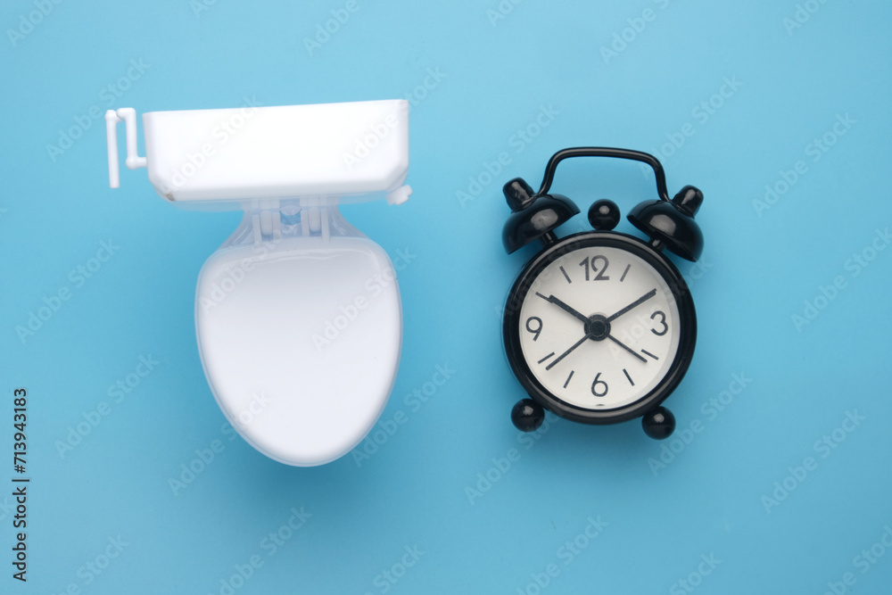 Flatlay picture of toilet bowl and alarm clock. Toilet break concept ...