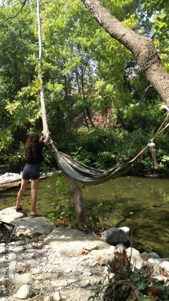 Vidéo Stock Young woman ties a hammock between trees in a campsite located in a dense forest by ...