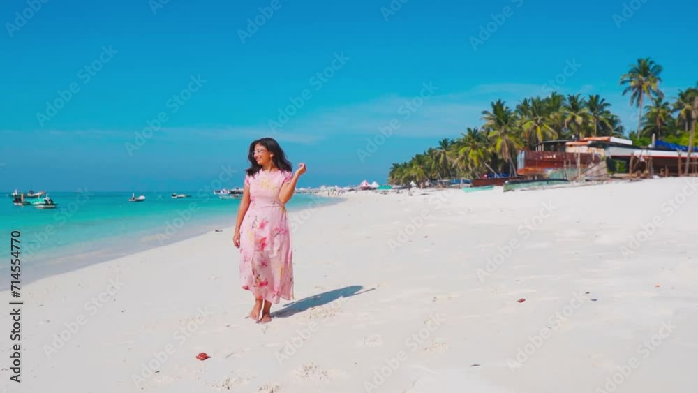 Beautiful Indian young woman in pink dress walking on white sand beach ...