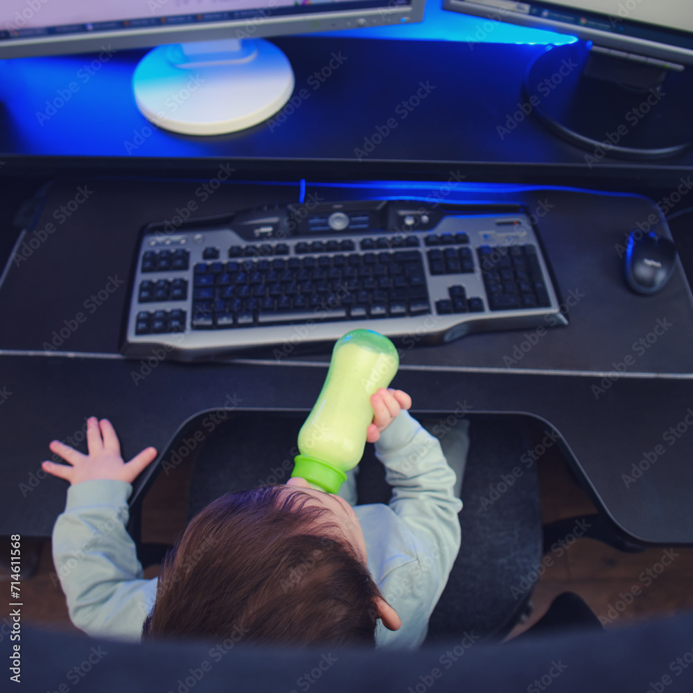 Happy baby is sitting at the computer keyboard with a bottle of milk in ...