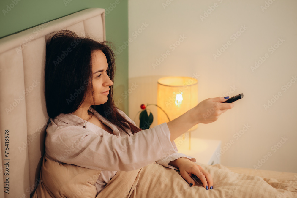 Attractive woman watching tv movie series sitting in bed, holding ...