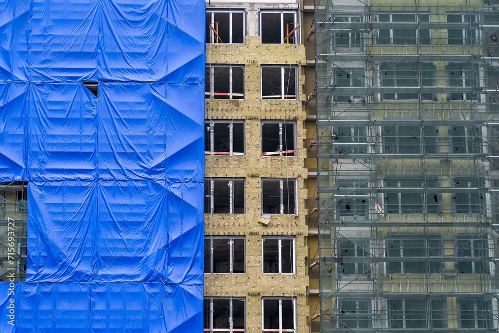 Building is under construction with blue tarps, external thermal ...