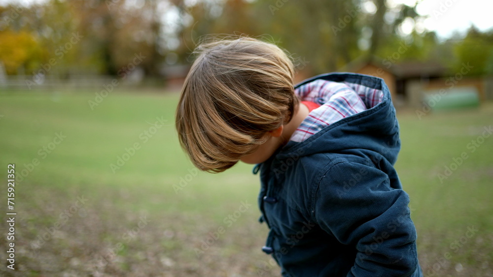 4 year old little boy walks in nature park outdoors looking down to ...