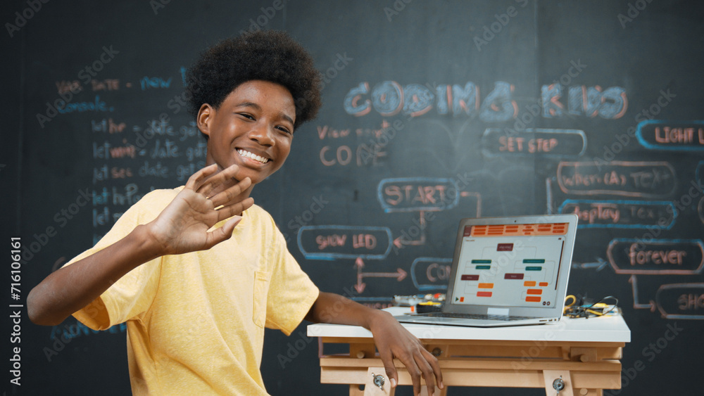 Smart african boy use laptop to code program and turn around to wave ...