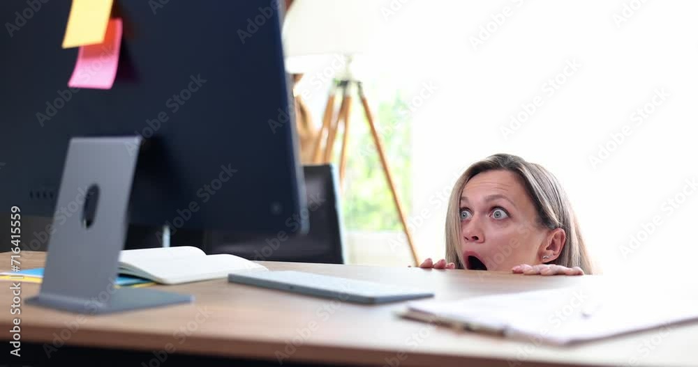 Woman looking at laptop computer from under desk frustrated shocked ...