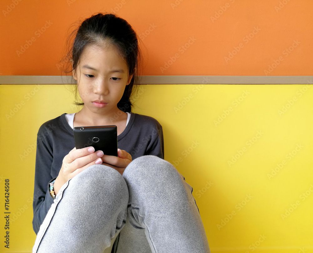 Asian child girl with serious face using smart phone too much screen ...