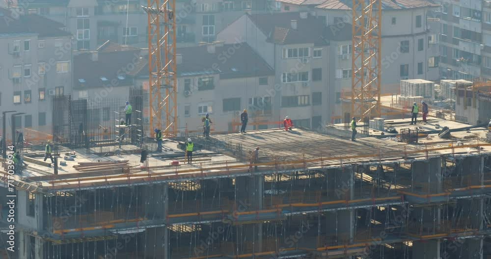 Construction workers labor on multi-story concrete building, telephoto ...
