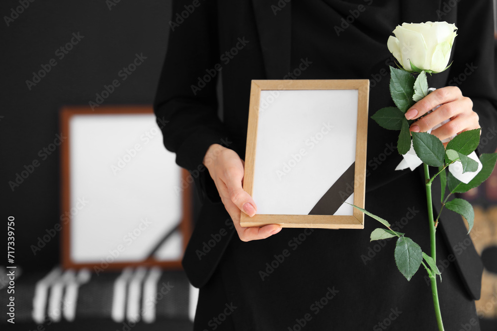 Grieving young woman with photo frame and rose at funeral, closeup ...