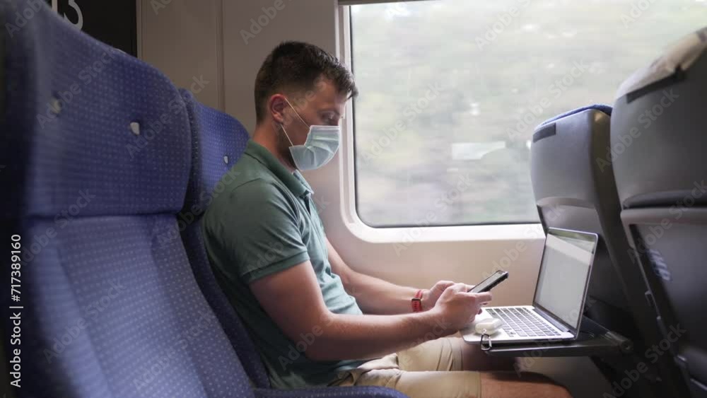 Man texting on phone holding laptop, commuter train in protective mask ...