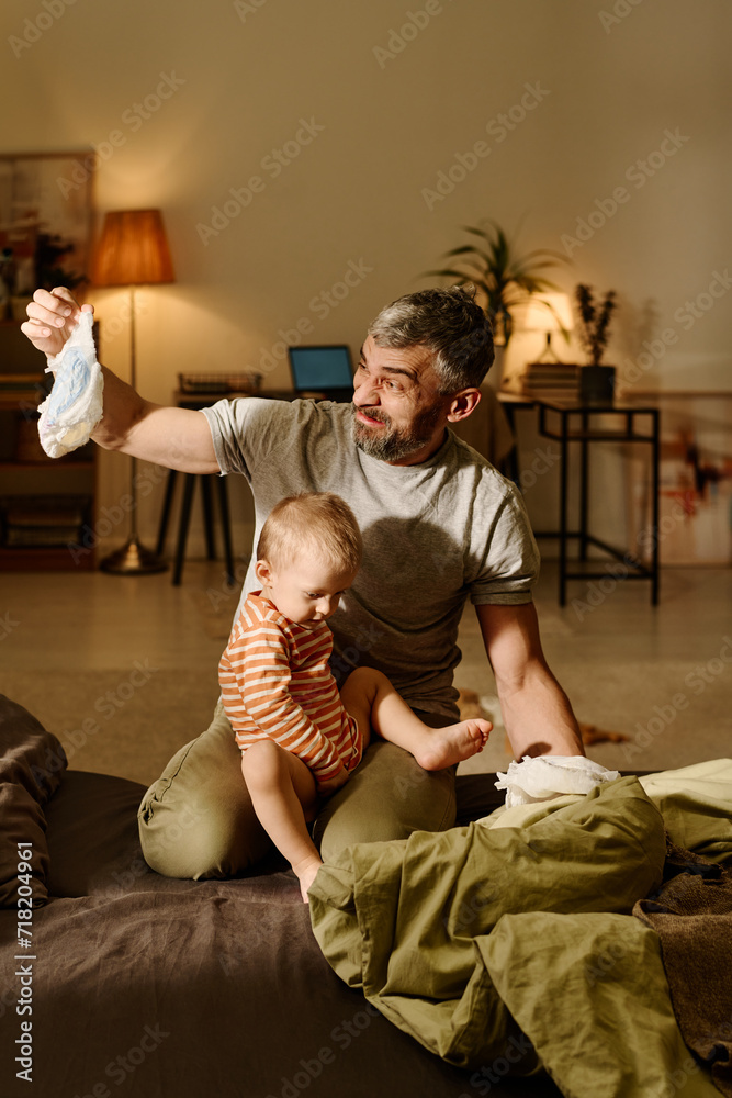 Disgusted father looking at dirty nappy of his baby son while sitting ...