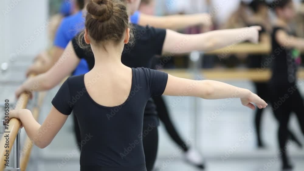 Little girl in a black leotard and bun is training curtsy at ballet ...