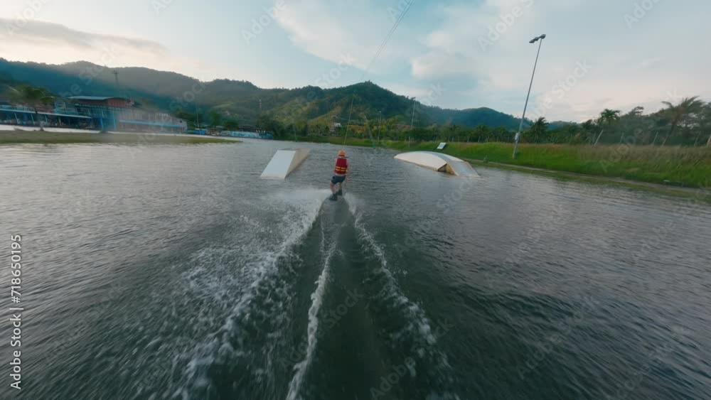 Beginner wakeboarder man in orange construction helmet trying cable ...
