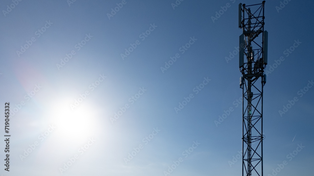 This image features a stark telecommunication tower silhouetted against a bright and clear sky ...