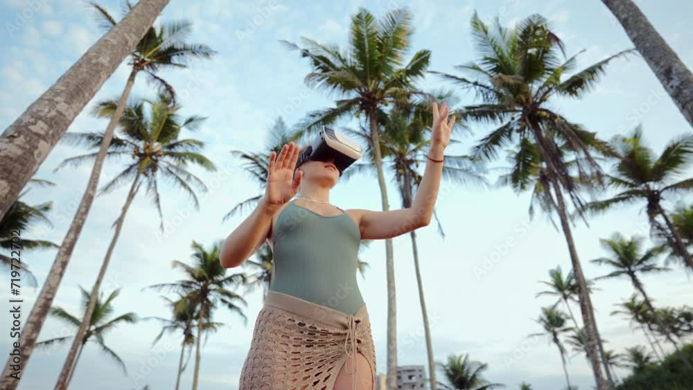 Woman in VR headset explores digital world among palm trees. Excited ...