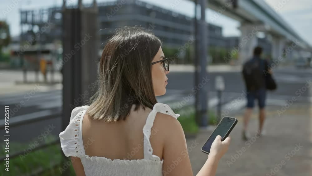 Beautiful hispanic woman in glasses, casually walking away, phone in hand along tokyo's modern ...