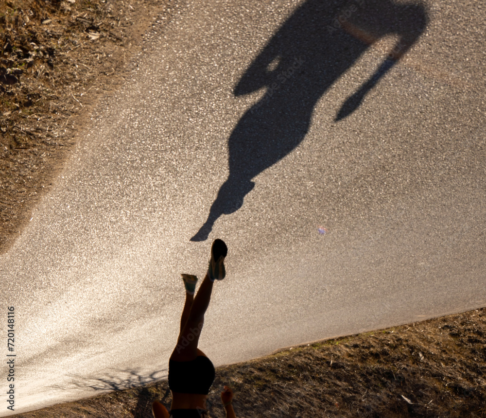 Shadow cast on a paved road of a fit young female runner running with a ...