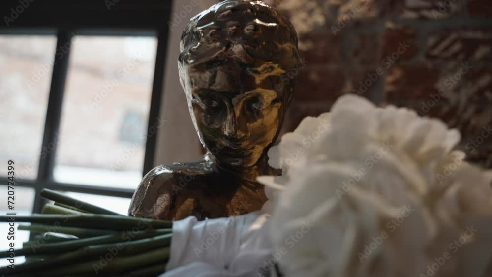 A metallic bronze bust of a woman with a serene expression is placed ...
