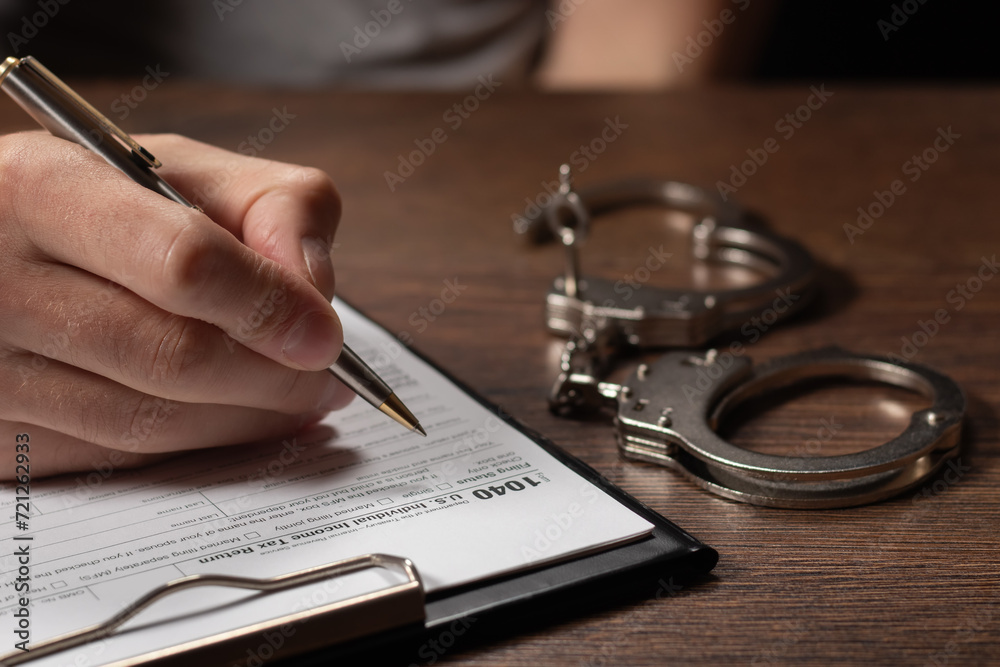 Tax evasion, crime and fraud concept. Man in handcuffs filling out tax ...