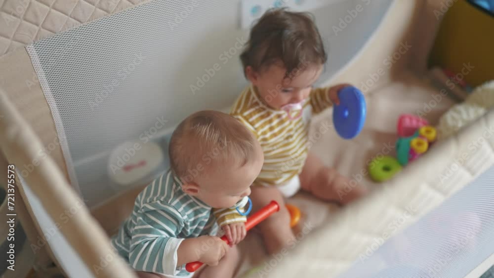 baby twins fight sitting in crib playpen. two baby toddlers are sitting ...