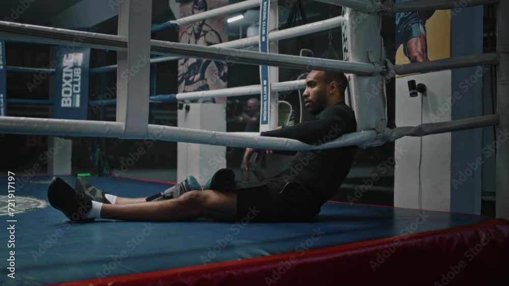 Tired and exhausted African American fighter sits in boxing ring corner ...