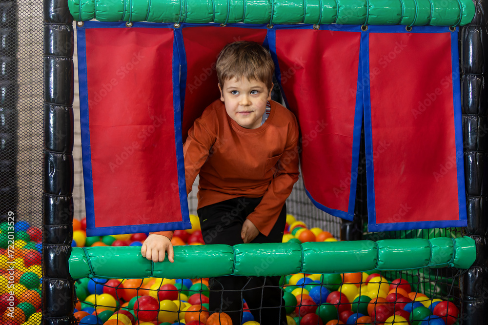Portrait of a cute boy looking through the entrance to ball pit in kids ...
