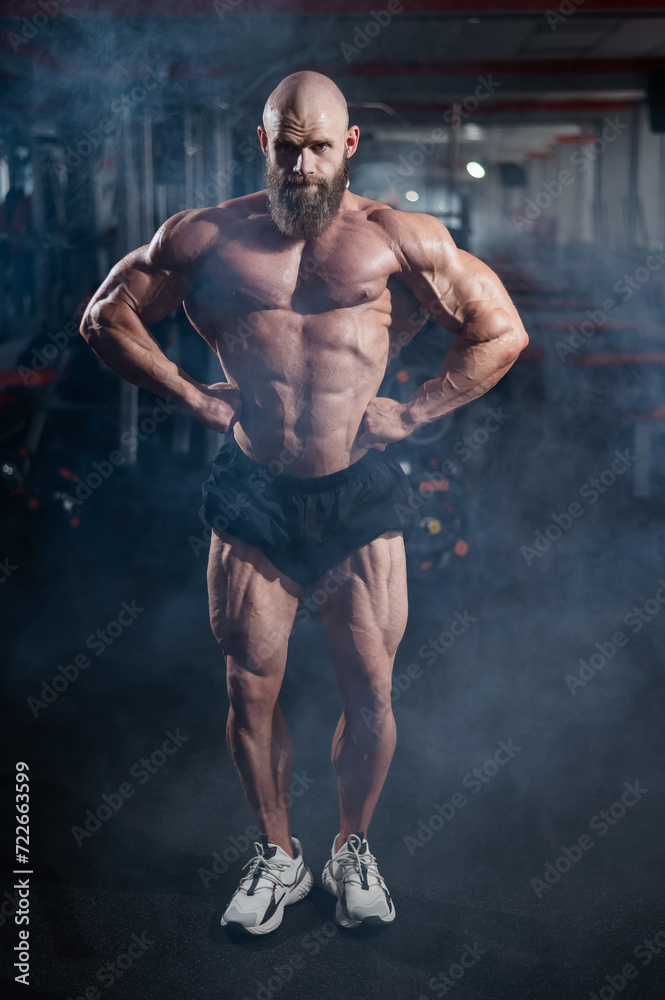 Muscular bald man posing in shorts. Bodybuilder showing off his shape in the gym. Stock Photo ...