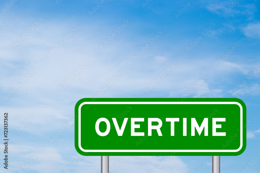 Green color transportation sign with word overtime on blue sky with ...