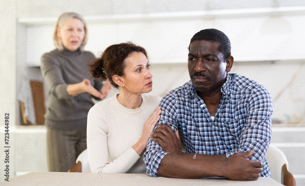 Middle-aged woman trying to calm angry man sitting at the kitchen table ...