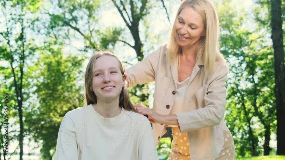 Mother shares tender moment with teenage daughter by gentle play with hair outdoor. Joy of ...