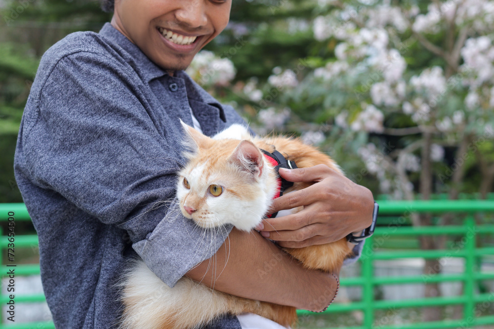 Outdoor portrait of Asian man holding and giving gentle touch to cat ...