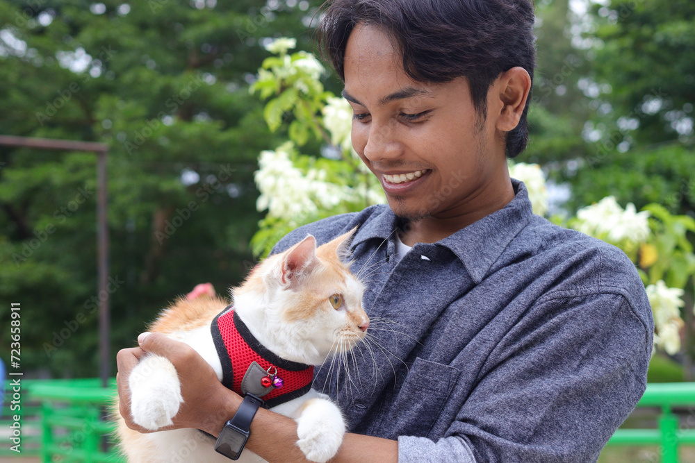 Outdoor portrait of Asian man holding and giving gentle touch to cat ...