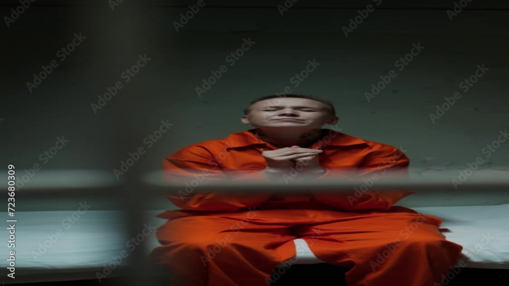 Vertical shot of female inmate in orange uniform sitting on bed in ...
