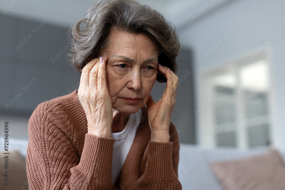 Sad, depressed senior woman sitting on sofa, touching her temples in ...
