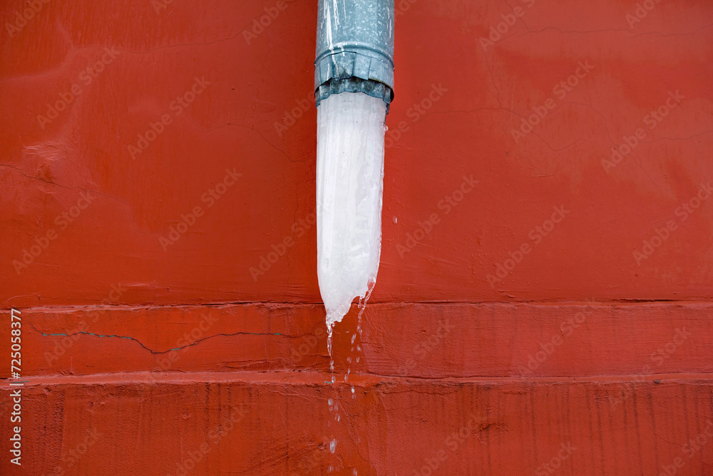 Icy drain pipes on red facade of the building. Ice block thaw in rain ...