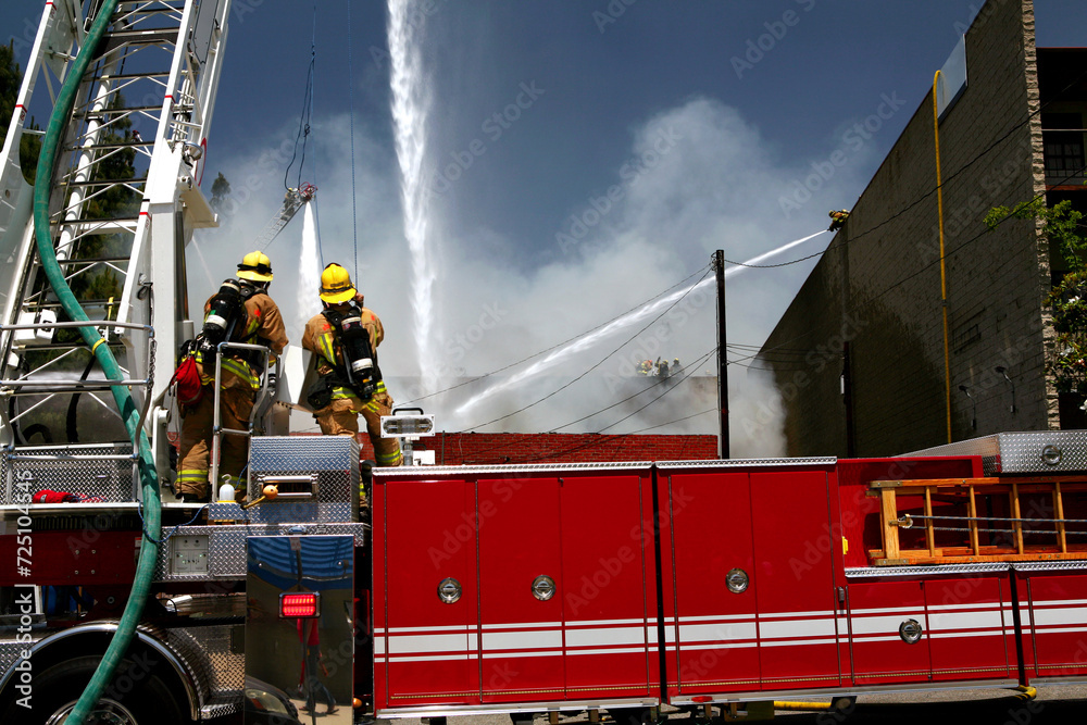 Horizontal image of Firefighters standing on a hook and ladder fire ...