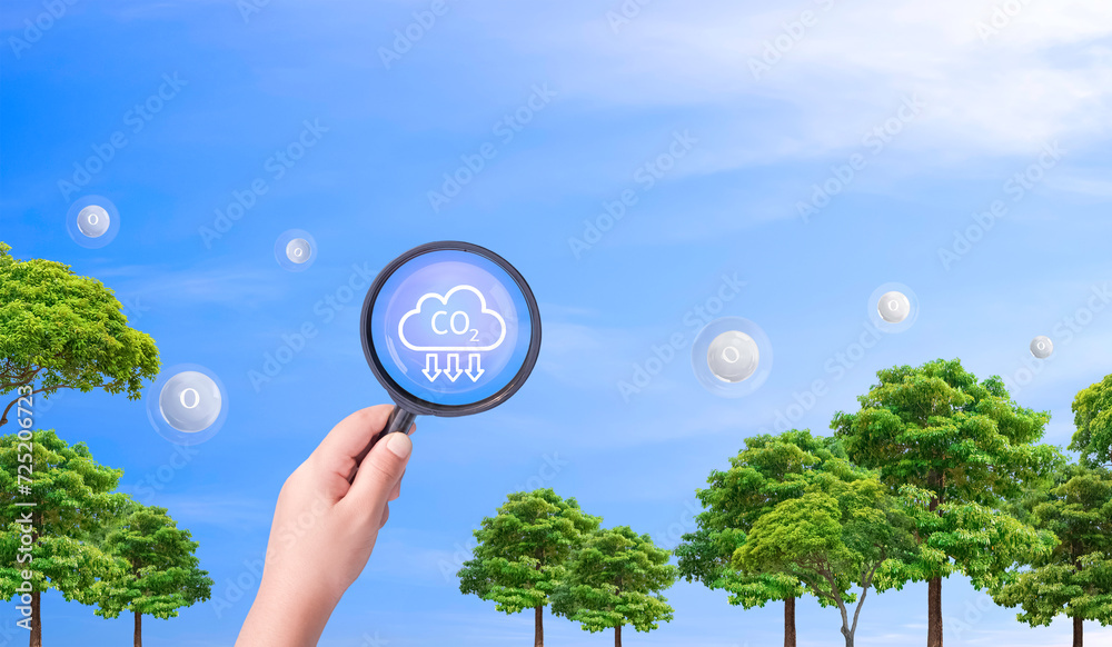 Hand holding magnifying glass with CO2 reduction icon and oxygen bubbles on the air in outdoors ...