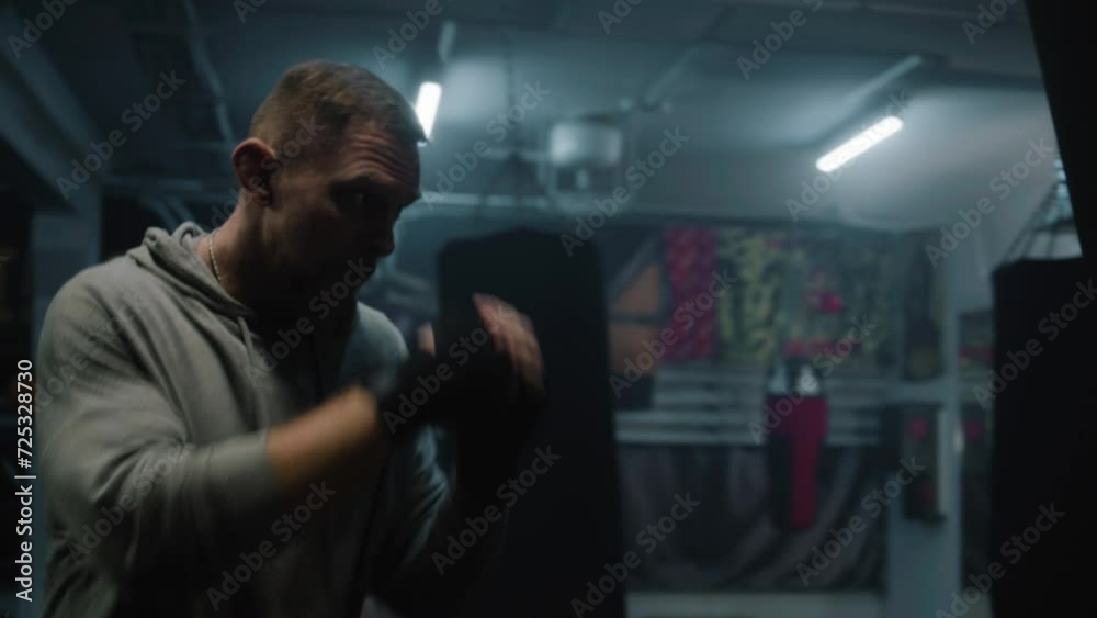 Stockvideon Male boxer in boxing bandages trains and hits punching bag ...