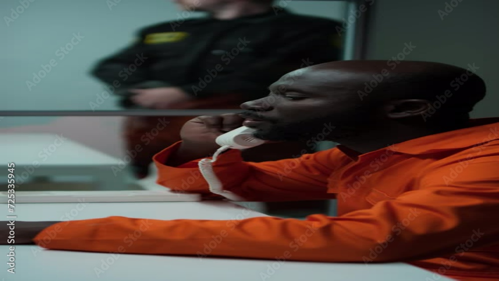 Vertical side view shot of Black inmate in prison uniform speaking on ...
