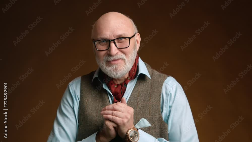 A man with a knowing smile clasps his hands together, hinting at a ...