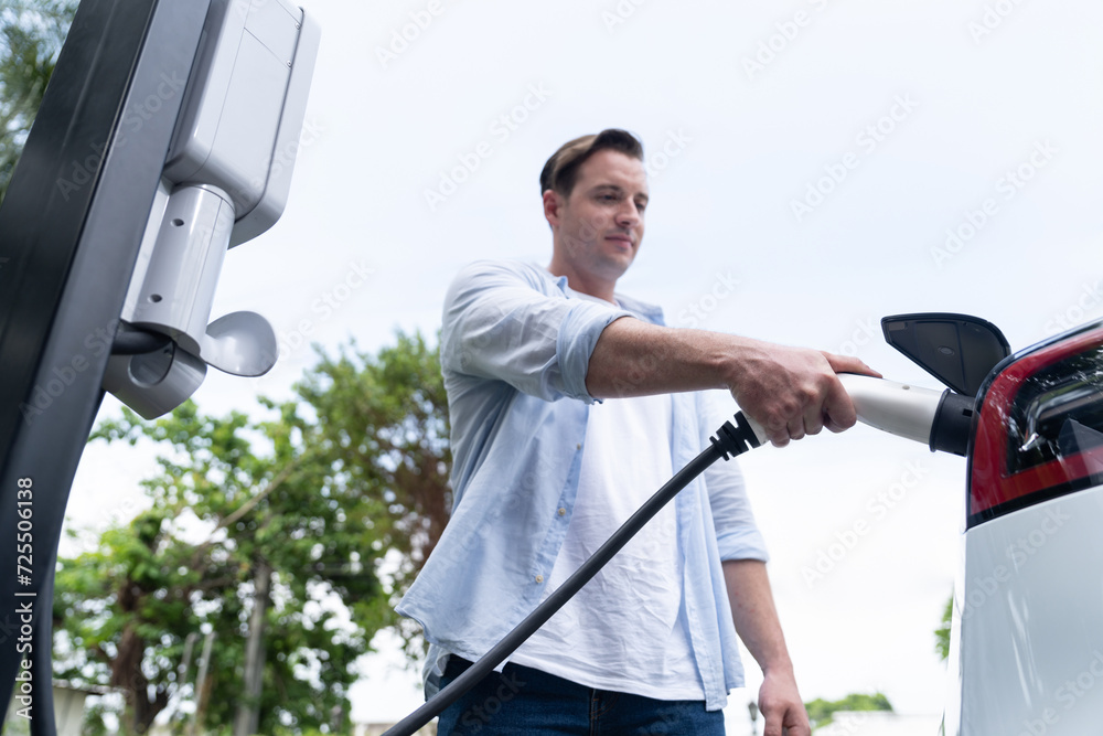 Eco-friendly conscious man recharging modern electric vehicle from EV ...