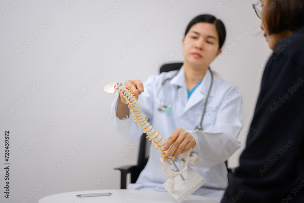 Asian female doctor points to spine model and explains female patient ...